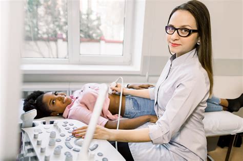 환자 복부와 내부 장기의 초음파 진단을 수행하는 여성 백인 의사 아프리카 소녀는 현대 병원의 초음파 진단 실에서 소파에 누워있다 2명에 대한 스톡 사진 및 기타 이미지