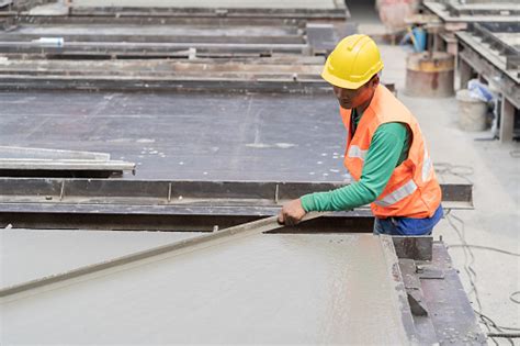 콘크리트 바닥을 매끄럽게 평평하게 하여 작업하는 건설 기술자 건설 노동자는 건설 현장에서 젖은 콘크리트를 붓는 긴 흙손을 사용합니다 콘크리트의 매끄러운 표면을 만드는 메이슨