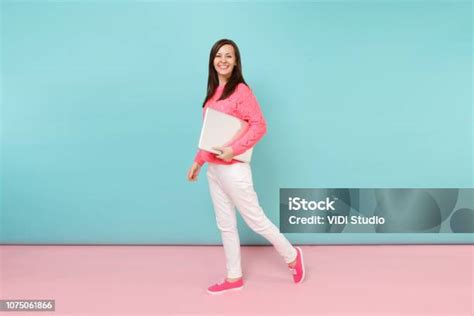 화이트 니트 장미 스웨터 바지 노트북 Pc 컴퓨터를 들고 있는 여자의 전체 길이 초상화 스튜디오에서 밝은 핑크 블루 파스텔 벽 배경에 고립 복사 공간을 조롱 하는 패션