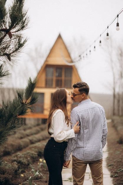 Casal Se Beijando Na Frente De Uma Casa Com Luzes Penduradas No Telhado