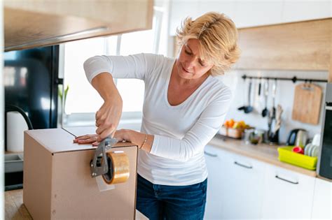 골판지 상자를 닫기 위해 접착제 테이프 디스펜서를 사용하는 여성 50 59세에 대한 스톡 사진 및 기타 이미지 50 59세 가정 생활 가정 주방 Istock