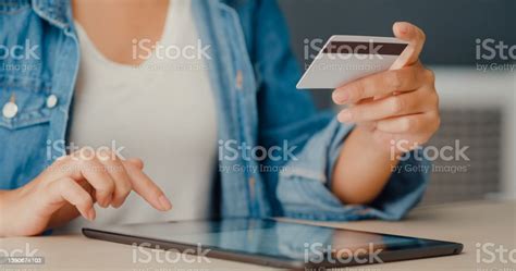 젊은 아시아 여성은 태블릿 주문 온라인 쇼핑 제품을 사용하고 거실 인테리어에서 신용 카드로 청구서를 지불합니다 집에 머물고 자가 격리 활동 코로나 바이러스 예방을위한 재미