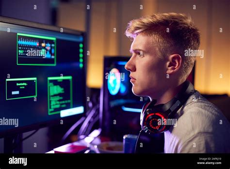 Male Teenage Hacker Sitting In Front Of Computer Screens Bypassing Cyber Security Stock Photo