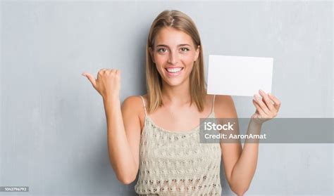 빈 카드 고 행복 얼굴 미소와 측면까지 손가락으로 보여주는 그런 지 회색 벽에 아름 다운 젊은 여자 가리키기에 대한 스톡 사진