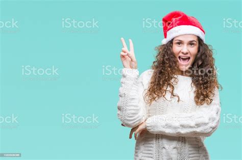 젊은 갈색 머리 여자 승리 표시를 하 고 카메라에 윙크 하는 행복 한 얼굴로 웃 고 고립 된 배경 위에 크리스마스 모자를 쓰고 번호 2입니다 겨울에 대한 스톡 사진 및 기타