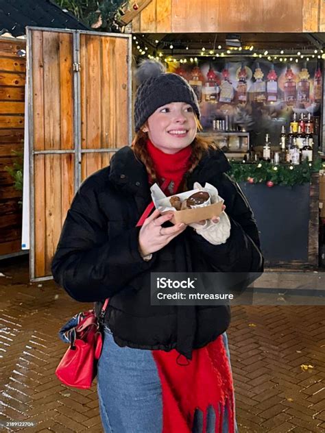 청바지 검은 패딩 재킷 빨간 스카프 니트 인조 모피 Bobble 모자를 입고 매력적인 빨간 머리 여자의 클로즈업 이미지 츄로와 초콜릿 스프레드의 골판지 트레이를 들고 야외
