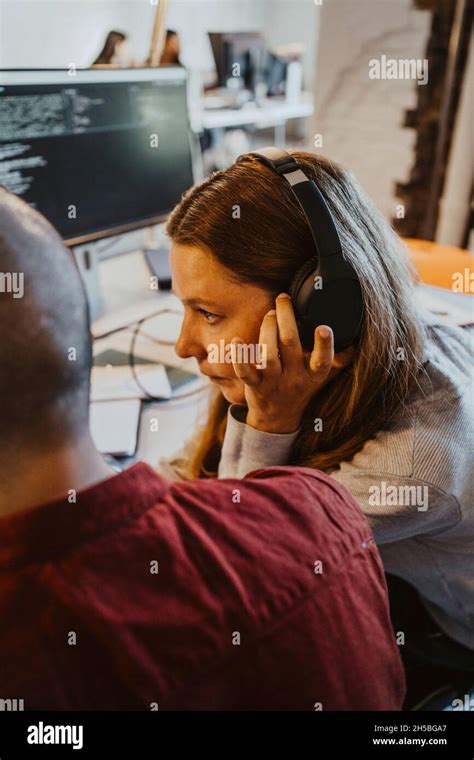 Female Programmer Listening Through Headphone While Doing Coding At