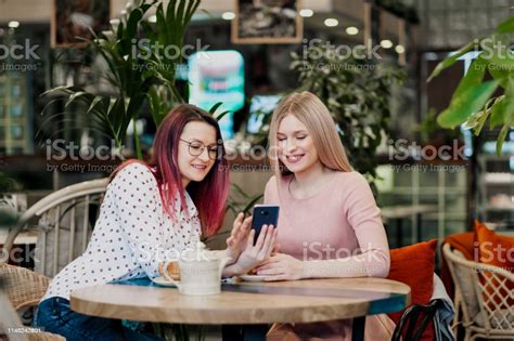 두 젊은 아름 다운 여자는 테이블에 녹색 카페에 앉아 크루아상으로 차를 마시고 채팅 하 고 웃 고 스마트폰에서 사진을 찍어 보세요 20 29세에 대한 스톡 사진 및 기타
