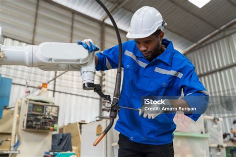 작업장에서 숙련된 로봇 팔과 함께 일하는 아프리카계 미국인 공장 남성 엔지니어 노동자 공장에서 남성 엔지니어 유지 보수 자동