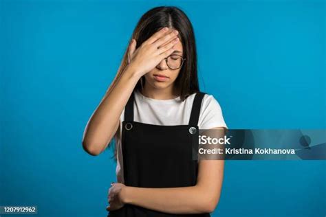 두통 스튜디오 초상화를 가진 긴 머리를 가진 젊은 학생 아시아 여자 파란색 배경에 고립 된 머리에 손을 얹는 소녀 문제와 두통의 개념 갈색 머리에 대한 스톡 사진 및 기타