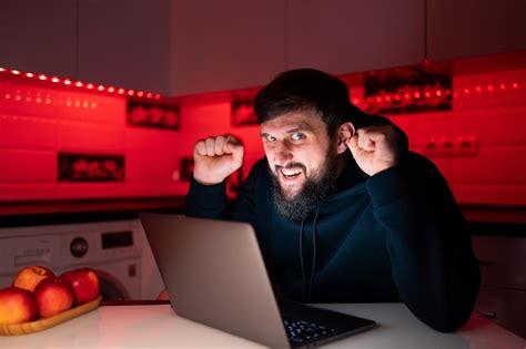 Premium Photo A Male Hacker Behind A Laptop In A Dark Room Raised His Fists Up