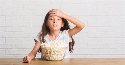 손으로 머리에 스트레스 팝 옥수수를 먹는 테이블에 앉아 젊은 히스패닉 아이 충격 수치심과 깜짝 얼굴로 분노와 좌절 두려워 하 고