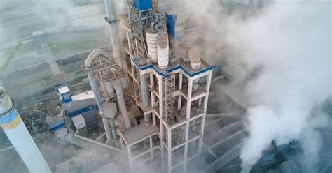 안개가 자욱한 저녁에 산업 제조 현장에서 높은 콘크리트 공장 구조와 타워 크레인이 있는 시멘트 공장의 조감도 생산 및 글로벌 산업 개념입니다 사진 Unsplash의