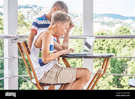 Brother Siblings Look Together At Difficult Game On Grey Laptop On Hotel Balcony Preteen