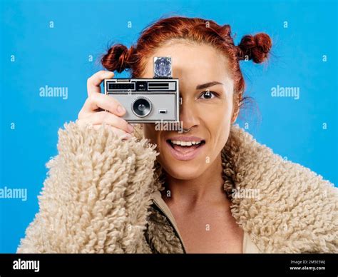 Beautiful Redhead Holding A Vintage Mm Camera With Cube Flash Over Blue Background Stock Photo