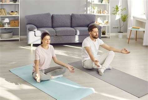 Husband And Wife Having Yoga Relaxation Practice In Brightly Lit Living