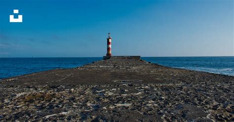 낮에는 푸른 하늘 아래 갈색 바위 해안의 빨간색과 흰색 등대 사진 Unsplash의 무료 바다 이미지