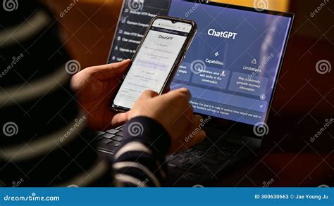 Computer Screen With ChatGPT Website And Person Using Mobile Phone To Ask Questions To ChatGPT