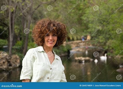 Beautiful Woman With Curly Hair Is Standing In Front Of A Pond Of Ducks