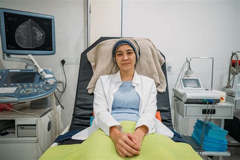 종양을 앓고있는 젊은 여성이 병원 침대에 누워 카메라를 보면서 반다나가 머리에 지쳐서 화학 요법 후 병원 병동에서 쉬고있는 아시아 중국 여성 환자에 대한 스톡 사진 및 기타