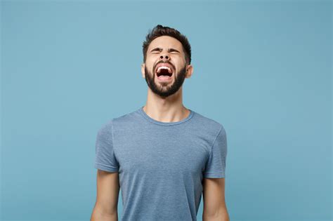 파란 벽 배경 스튜디오 초상화에 고립 된 포즈 캐주얼 옷에 젊은 좌절 미친 남자 사람들은 진지한 감정 라이프 스타일 개념 복사 공간을 모의합니다 눈을 감고 비명을 지르며 T