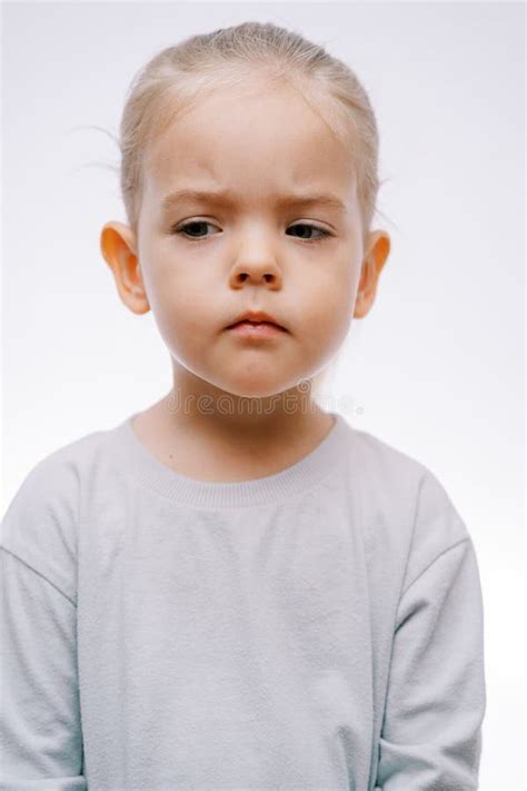 Portrait Of A Little Pensive Girl With Raised Eyebrows On A Gray