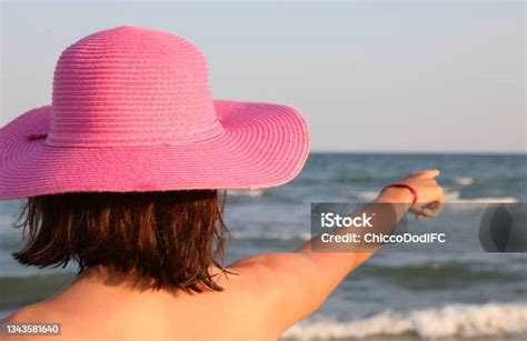바다 한가운데지점을 가리키는 큰 밀짚 모자를 쓰고 뒤에서 온 젊은 여성 나이에 대한 스톡 사진 및 기타 이미지 나이 모자