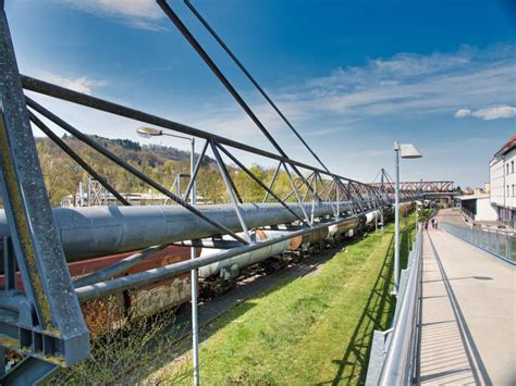 Sunny Sidewalk With Grass And A Long Pipe Running Along It Under A Blue