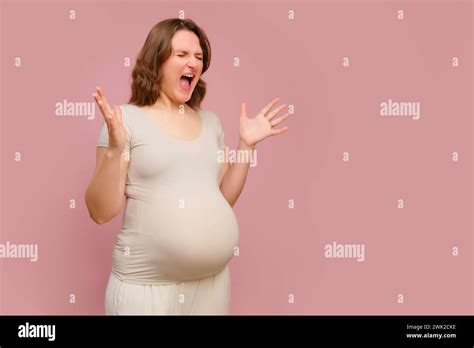 A Screaming Pregnant Woman On A Studio Pink Background Pregnancy In A