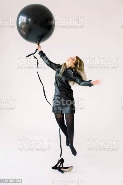점프하고 비행하는 동안 큰 검은 공기 풍선을 들고 검은 드레스에 쾌활한 어린 소녀의 전체 길이 초상화 흰색 배경 위에 고립 된 카메라를보고 거리에 대한 스톡 사진 및 기타