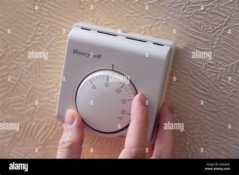 A Woman S Hand Turning A Temperature Dial On A Honeywell Thermostat In