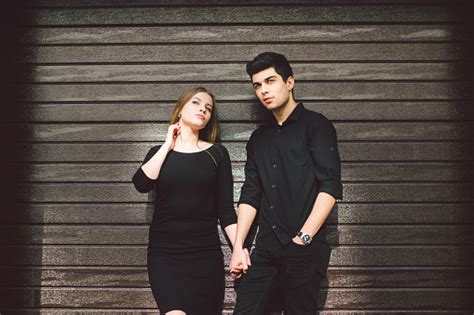 나무 벽의 배경에 함께 서 매력적인 혼합 인종 커플의 초상화 데이트 검은 옷을 입고 다민족 세련된 젊은 부부는 야외에서 함께 시간을 보내고있다 2명에 대한 스톡 사진 및