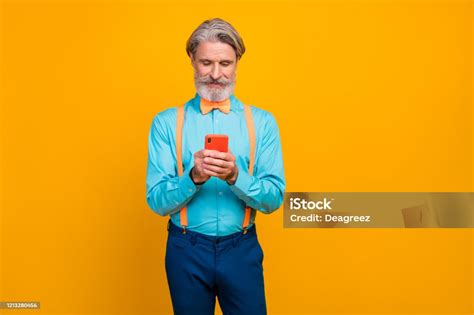 유행 펑키 할아버지 쓰기 전화 새로운 흥미로운 블로그 게시물 시니어 인기 테마 착용 블루 셔츠 서스펜더 나비 넥타이 바지 고립 된 노란색 색상 배경의 사진 성년 남자에 대한