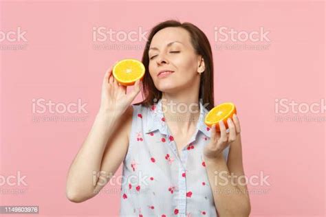 여름 옷에 예쁜 젊은 여성이 분홍색 파스텔 배경에 고립 된 신선한 잘 익은 오렌지 과일의 Halfs를 들고 눈을 유지 사람들은 생생한 라이프 스타일 휴식 휴가 개념입니다