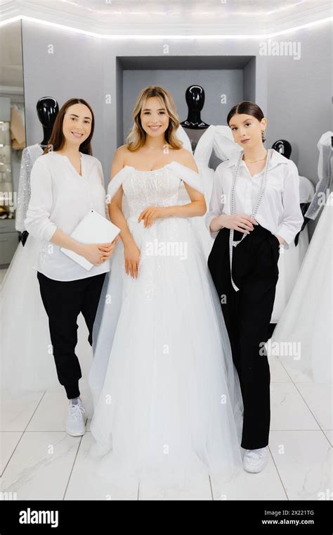 The Bride To Be Chooses A Dress For The Wedding A Dressmakers Assistant Is Fitting A Dress For