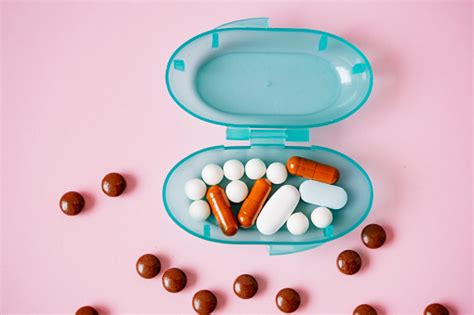 강렬한 분홍색 표면 위에는 다양한 알약과 매혹적인 초콜릿 볼로 가득 찬 파란색 용기가 있어 건강과 사치의 흥미로운 시각적 조합을 만들어냅니다 건강관리와 의술에 대한 스톡