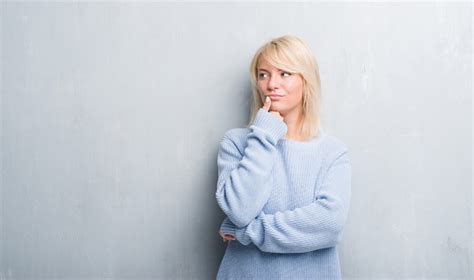 성인 질문 잠겨있는 표현에 대 한 친 생각에 손으로 겨울 스웨터를 입고 그런 지 회색 벽에 백인 여자 사려깊은 얼굴 미소 의심 개념입니다 가을에 대한 스톡 사진 및 기타