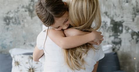 매력적이고 웃는 어린 딸은 집에서 함께 자유 시간을 보내는 동안 사랑하는 어머니를 안아줍니다 여자는 카메라에 등을 대고 앉아 어린 소녀를 껴안는다 사진 Unsplash