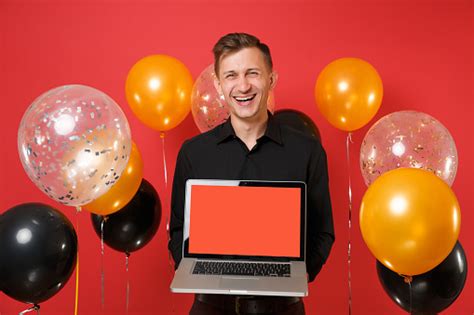 블랙 클래식 셔츠 빨간색 배경 공기 풍선에 빈 검은색 빈 화면으로 노트북 Pc 컴퓨터를 들고 젊은 남자를 웃 고 있다 여자의 날 해피 뉴가 어 생일 이랑 휴일 파티 개념