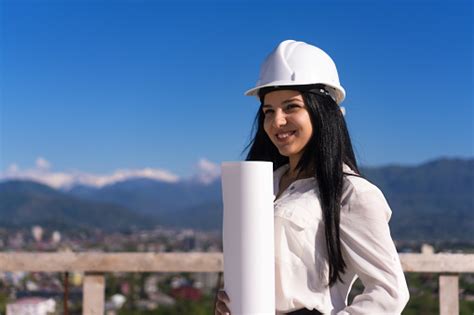 맑은 날 산을 배경으로 손에 그림을 들고 건설 현장에서 안전모를 쓴 젊은 여성 엔지니어 건설 검사관 25 29세에 대한 스톡 사진 및 기타 이미지 Istock