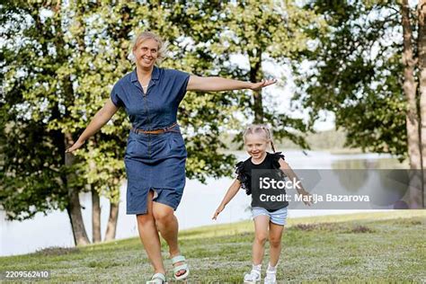 엄마와 딸은 호수 근처 잔디밭을 걷고 균형을 잡고 야외에서 화창한 날을 즐기고 자연 속에서 가족과 함께 시간을 축하합니다 2 3 살에 대한 스톡 사진 및 기타 이미지