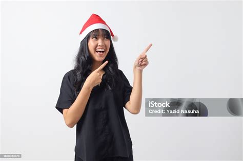 빨간 산타 모자를 쓴 매력적인 아시아 여성의 초상화가 행복 한 느낌 손가락으로 제품을 가리키고 보여주는 모습 새해와 크리스마스 컨셉입니다 흰색 배경에 고립된 이미지 12월에