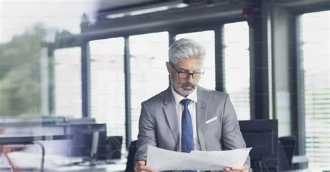 회색 양복을 입은 성숙한 사업가가 사무실 책상에 앉아 문서를 읽고 있다 사진 Unsplash의 사업 이미지