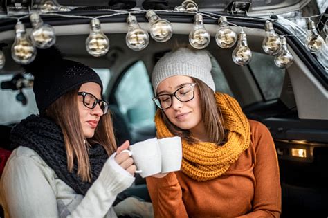 겨울에 야외에서 차를 마시는 두 명의 아름다운 젊은 여성 그들은 차의 트렁크에 앉아 겨울날에 뜨거운 차를 즐길 수 있습니다 18 19세에 대한 스톡 사진 및 기타 이미지