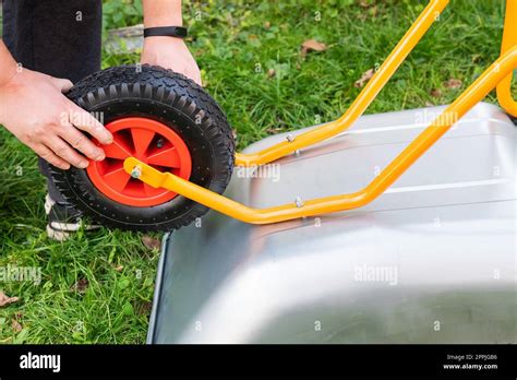 There Is A Metal Wheelbarrow On The Street A Man Spins A New Wheelbarrow For Work Tightens