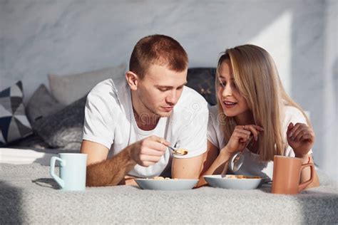 Una Pareja Joven Y Encantadora Desayuna En Casa Mientras Se Acuesta En La Cama Foto De Archivo