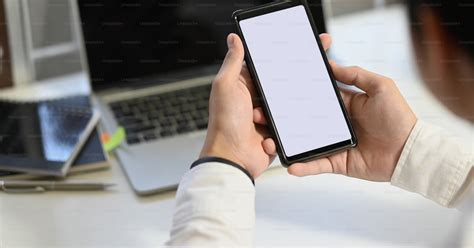 흐릿한 노트북과 사무 장비를 배경으로 한 현대적인 작업 책상에서 흰색 빈 화면이 있는 자르기 검은색 스마트폰을 들고 있는 사업가의 손이 잘린 사진 사진 Unsplash