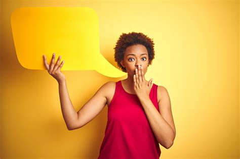 노란 고립 된 배경 커버 입 에 연설 거품을 들고 젊은 아프리카 계 미국인 여성 실수 두려움의 표현 침묵 비밀 개념에 대 한 수치와 충격 가리기에 대한 스톡 사진 및 기타
