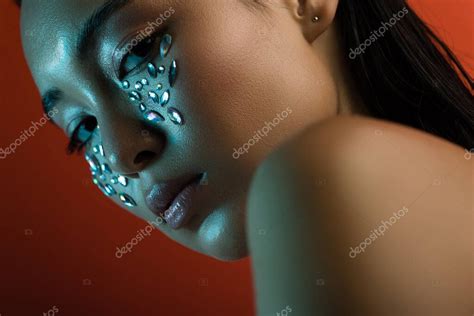 hermosa chica asiática desnuda con diamantes de imitación brillantes en la cara mirando a la