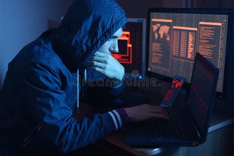 hacker in hood typing program code while committing a cybercrime